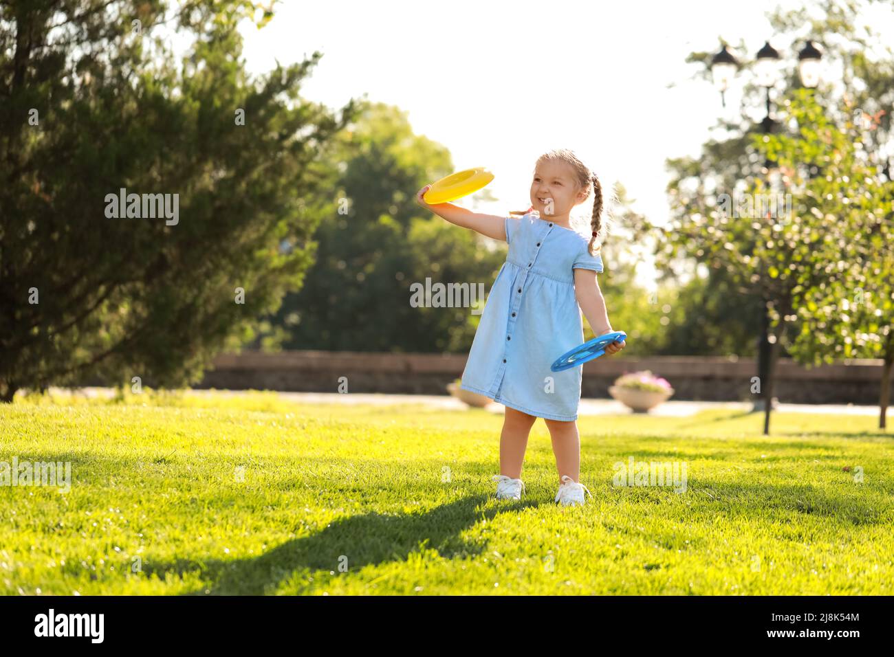 Cute little girl in blue dress catching frisbee in park Stock Photo - Alamy
