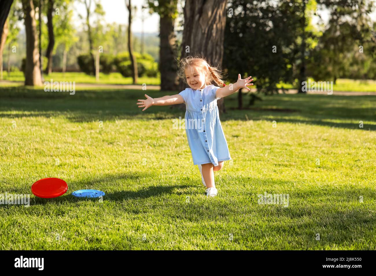 Cute little girl in blue dress playing frisbee in park Stock Photo - Alamy