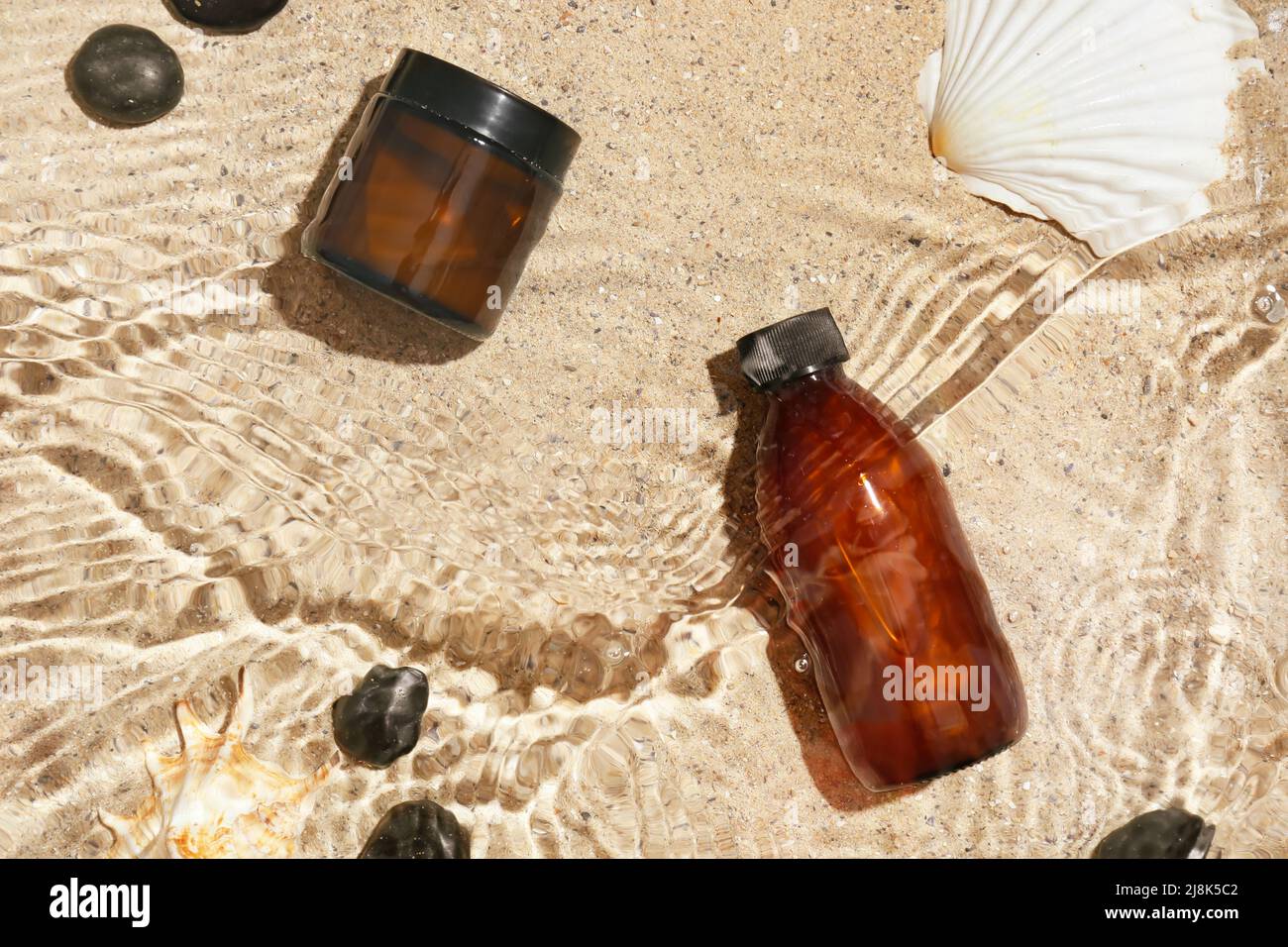 Cosmetic products and spa stones in water on sand Stock Photo - Alamy