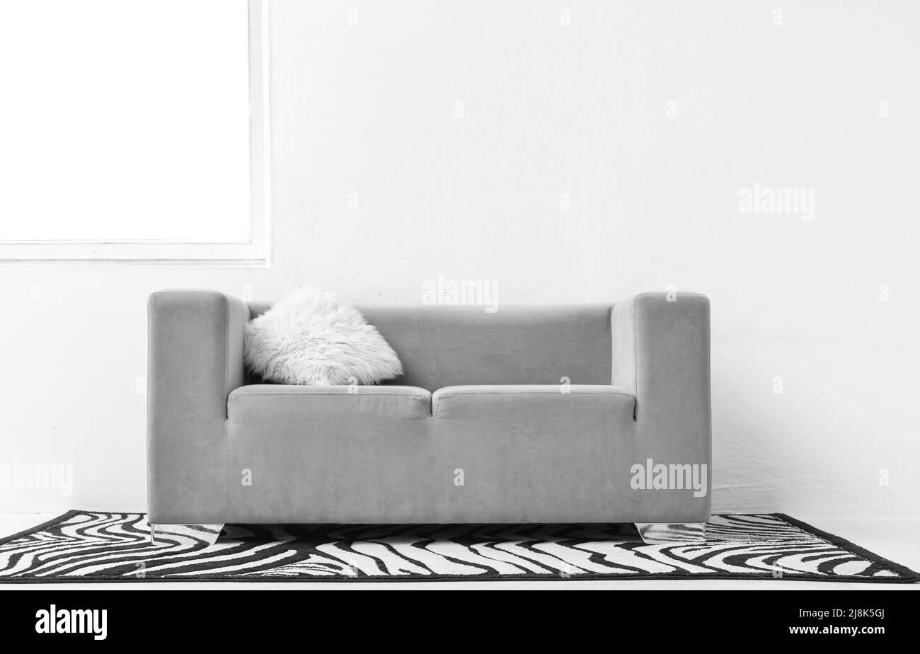Grey sofa with cushion and carpet near light wall Stock Photo - Alamy