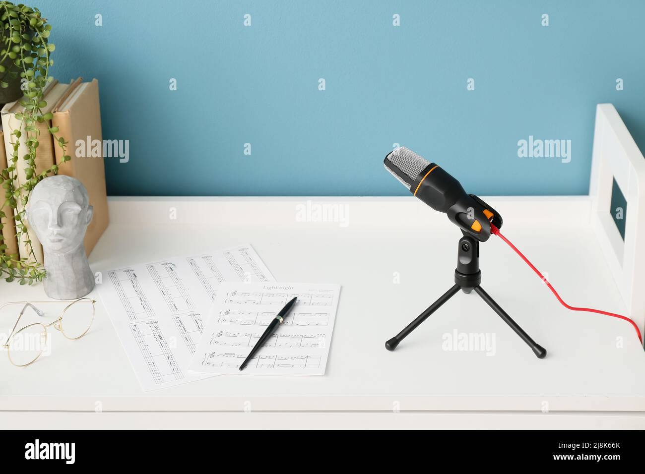 Sheets of music and professional microphone on table near color wall ...