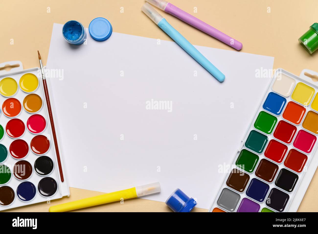 Blank paper sheet with paints and felt-tip pens on beige background ...