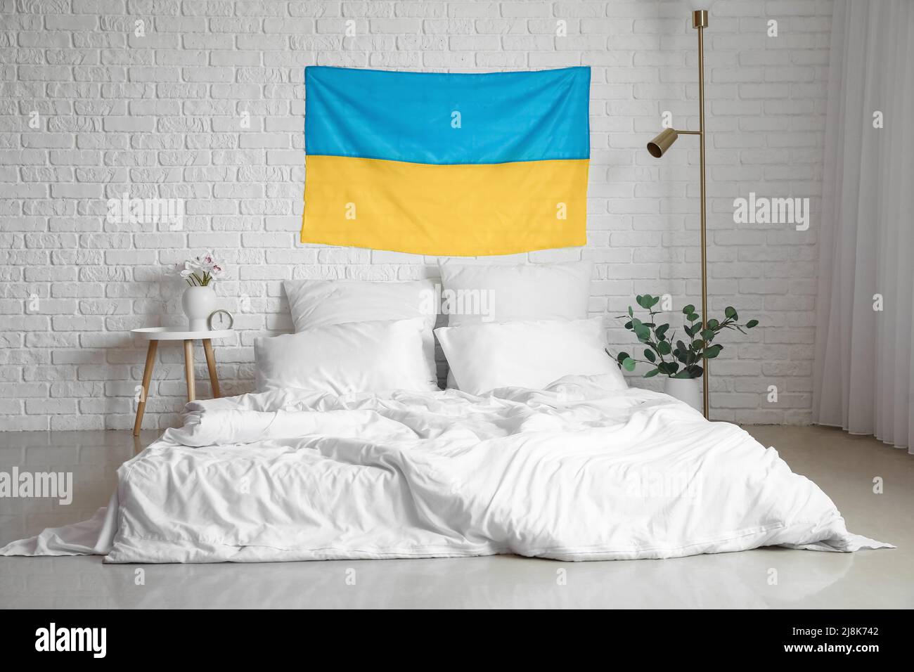 Interior of light bedroom with flag of Ukraine and comfortable bed ...