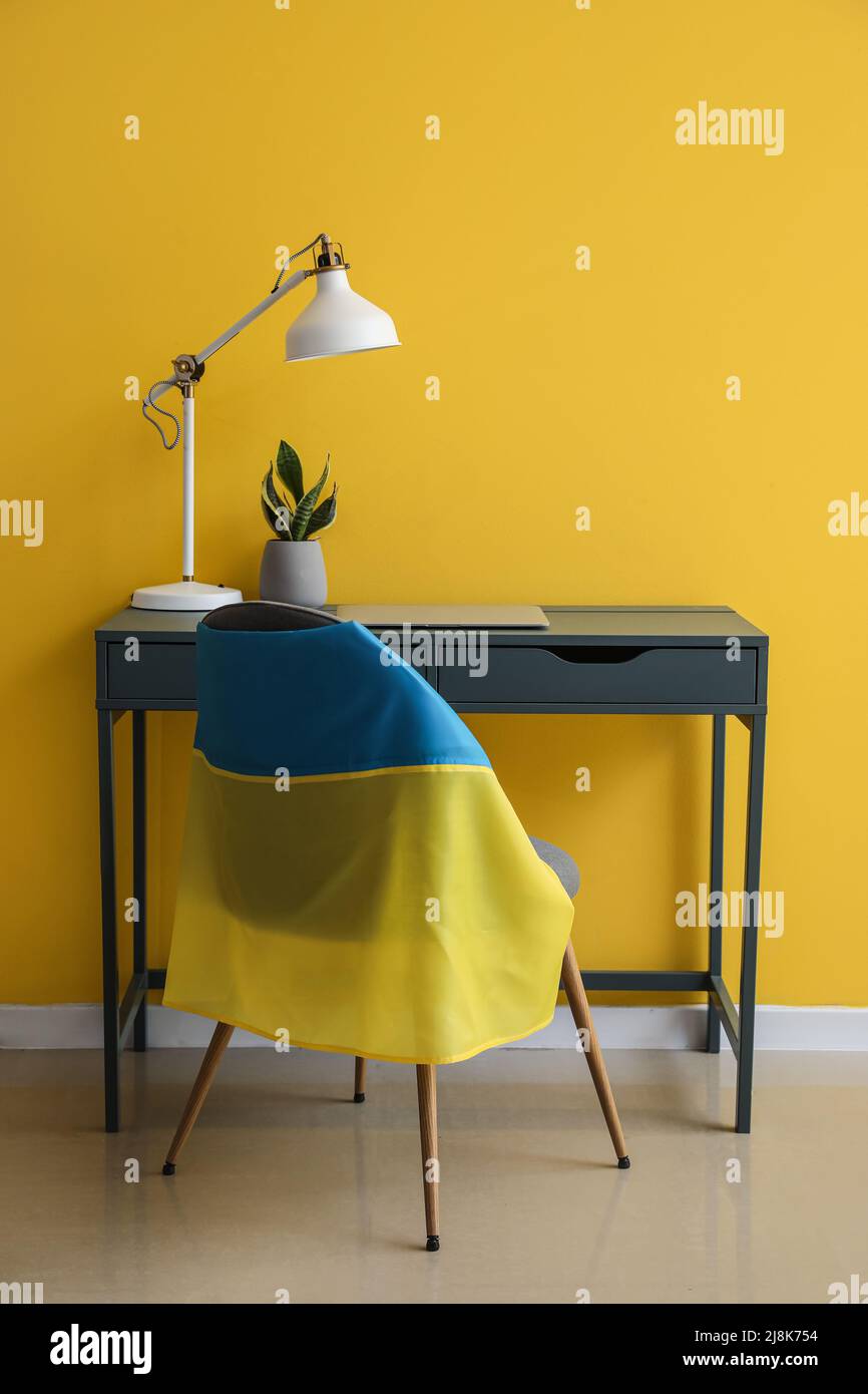 Workplace with modern laptop and flag of Ukraine on chair near color ...