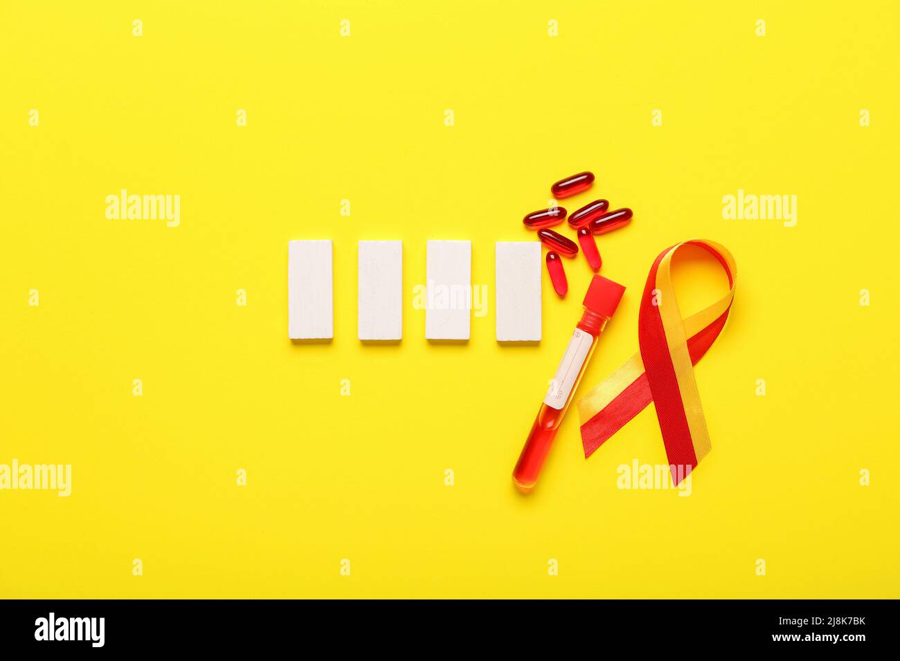 Awareness ribbon with blood sample, pills and blocks on yellow ...