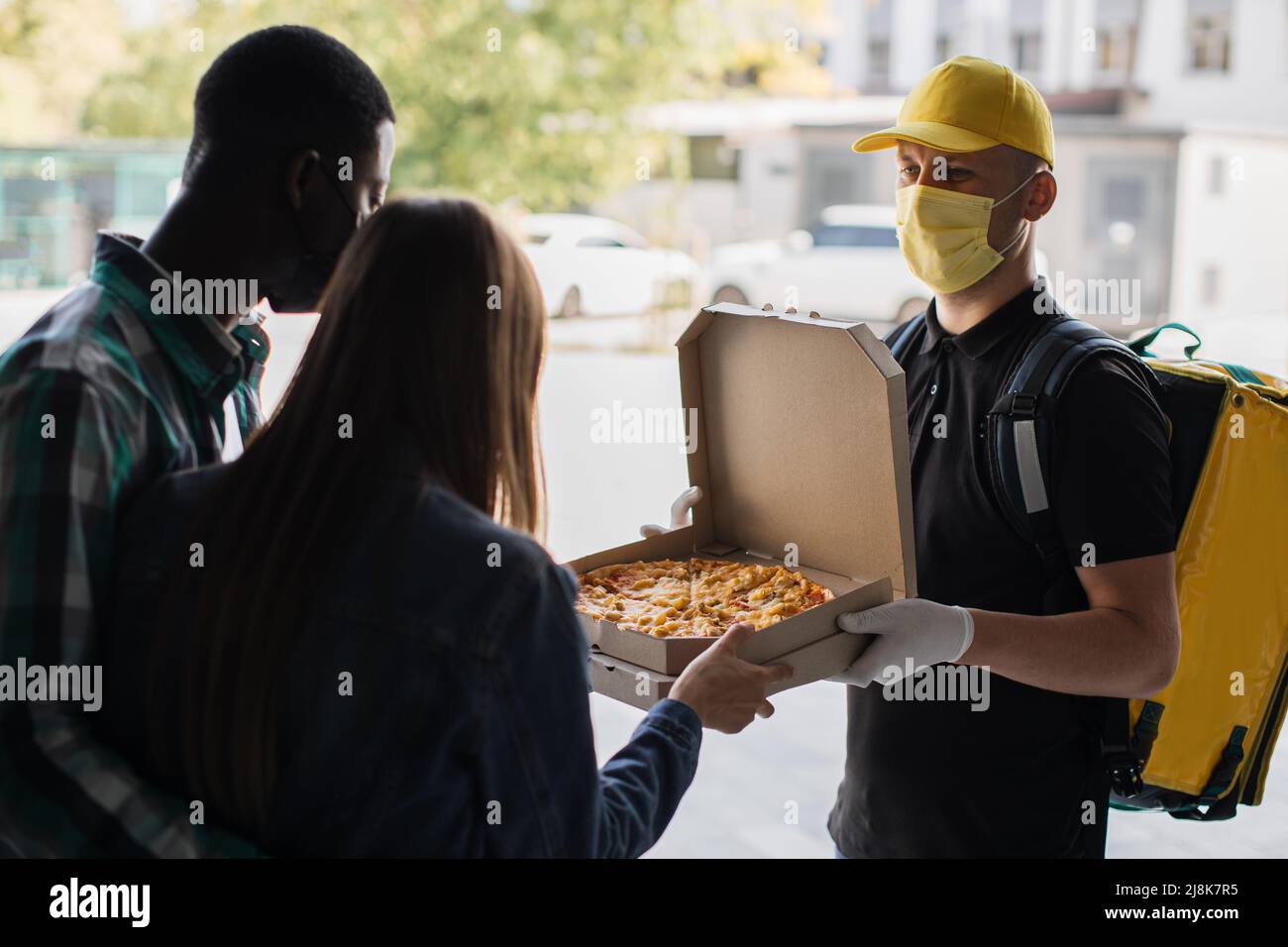 Smilling delivery man in yellow face mask, uniform cap delivering ...