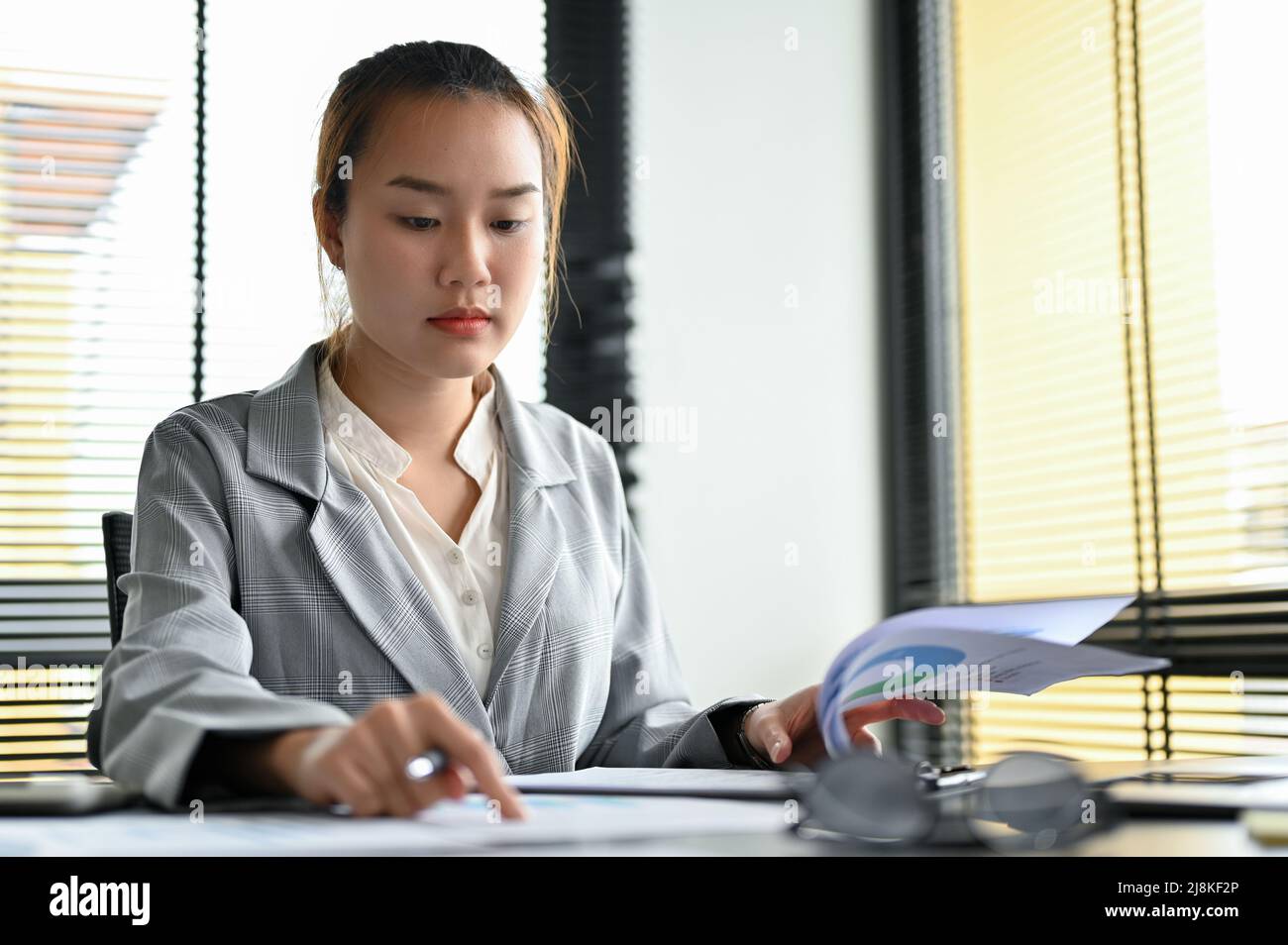 Millennial Asian businesswoman concentrates on her work assignment ... Millennial Asian businesswoman concentrates on her work assignment ...
