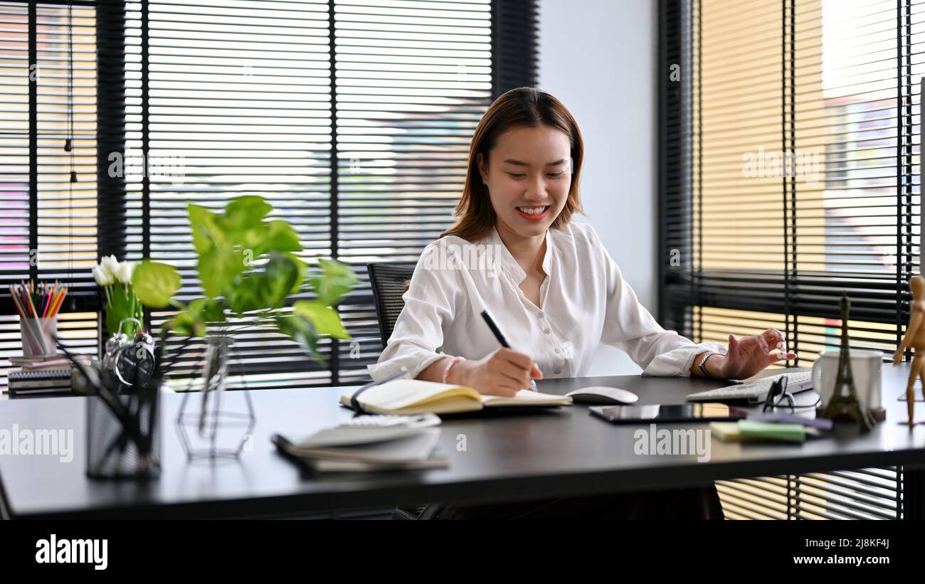 Cheerful Asian female manager sits at her desk in a private office ...