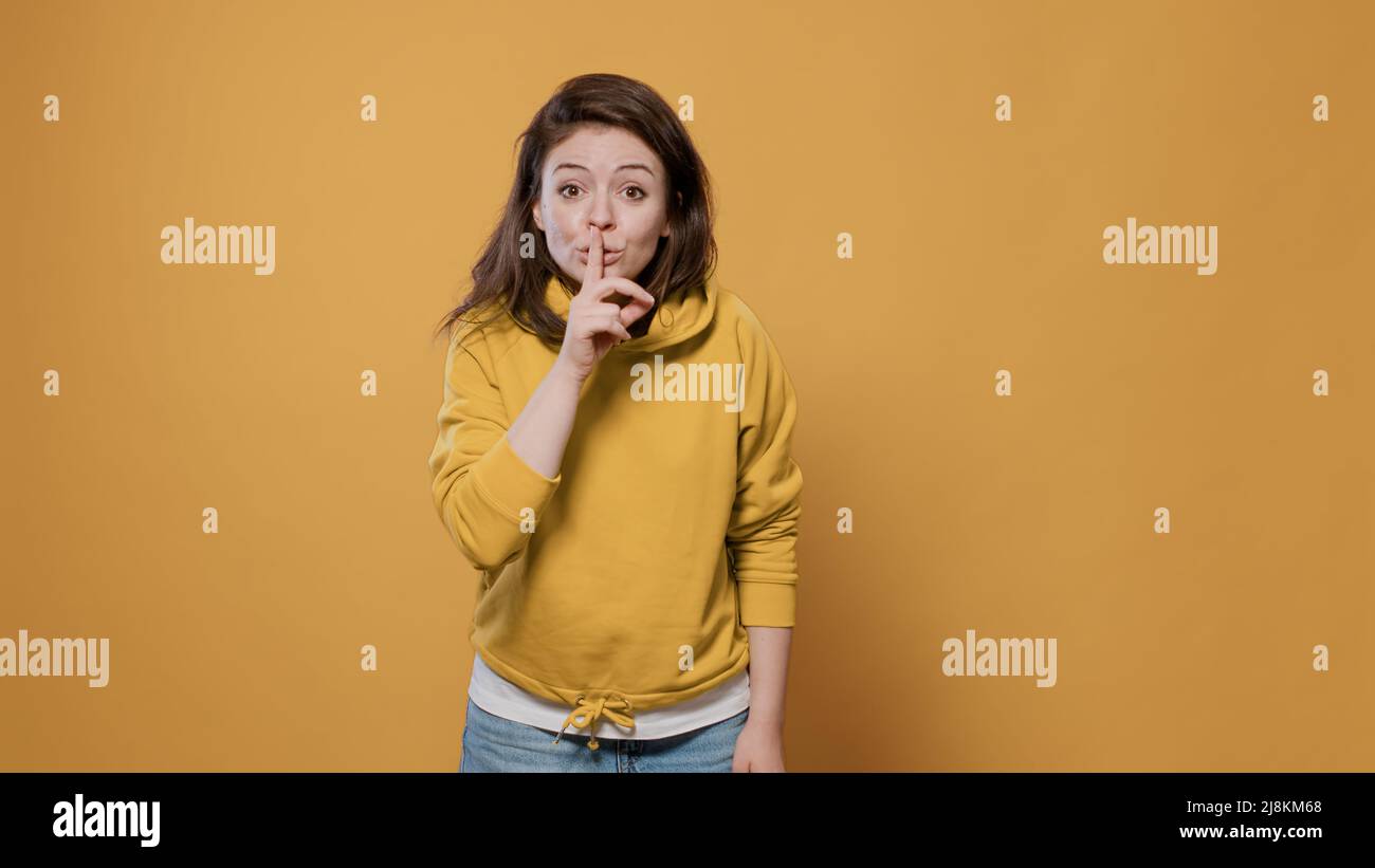 Casual woman wearing hoodie putting index finger over lips doing silent ...