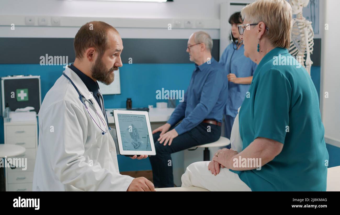 Male osteopath showing human skeleton illustration on tablet ...