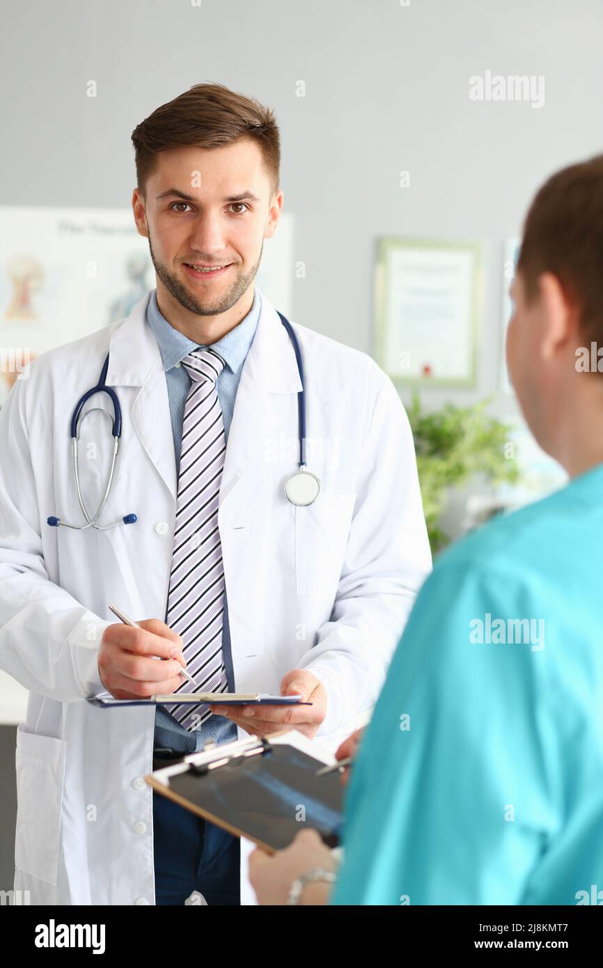 Head doctor in medical gown hold patient medical history, intern write ...