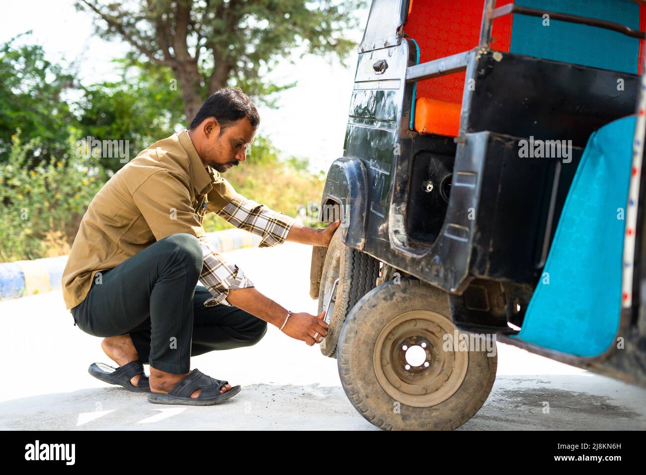 Auto driver changing punctured wheel on roadside while riding - concept ... Auto driver changing punctured wheel on roadside while riding - concept ...