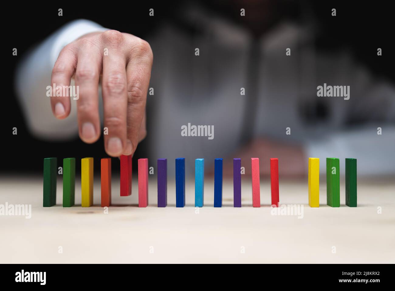 Conceptual photo of a hand placing a stone to a row of domino stones ...