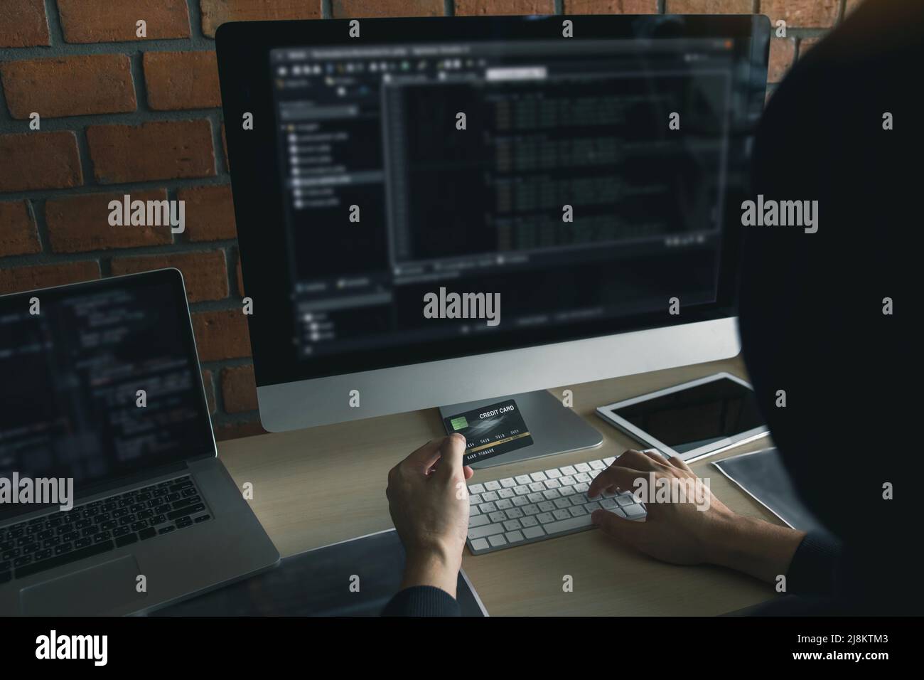 Hacker in the hood working with computer and holding credit card with ...