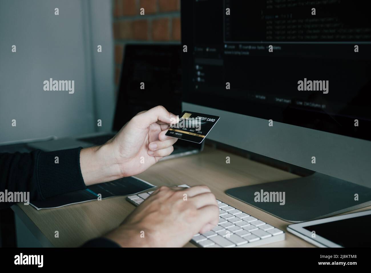 Hacker in the hood working with computer and holding credit card with ...