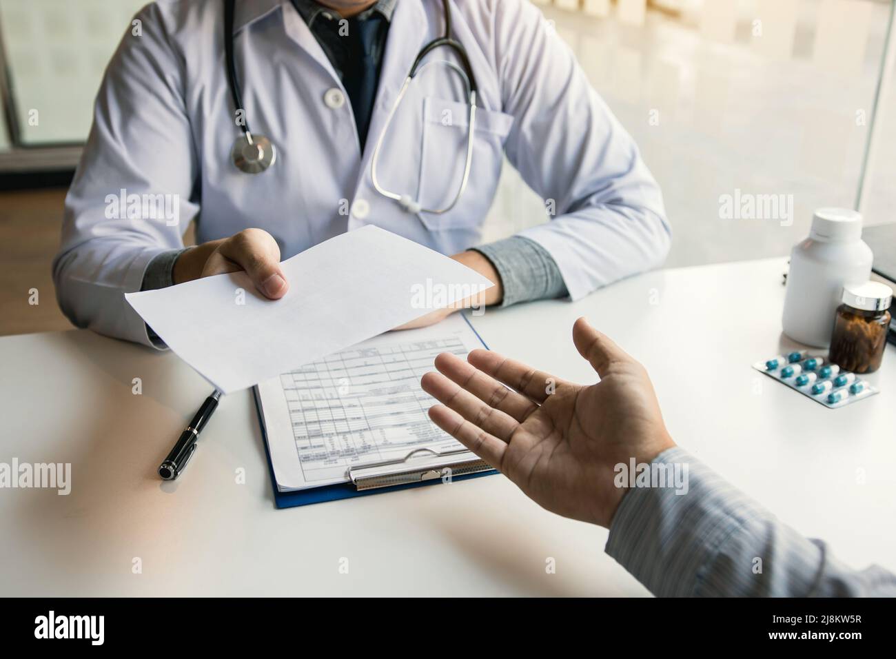 Asian male doctor talking in clinic room and handing a prescription to ...