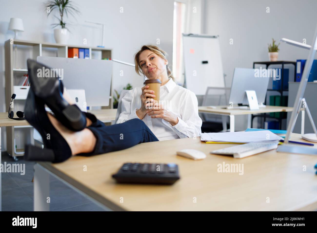 Business woman with hot coffee cup put her legs on the desk resting in ...