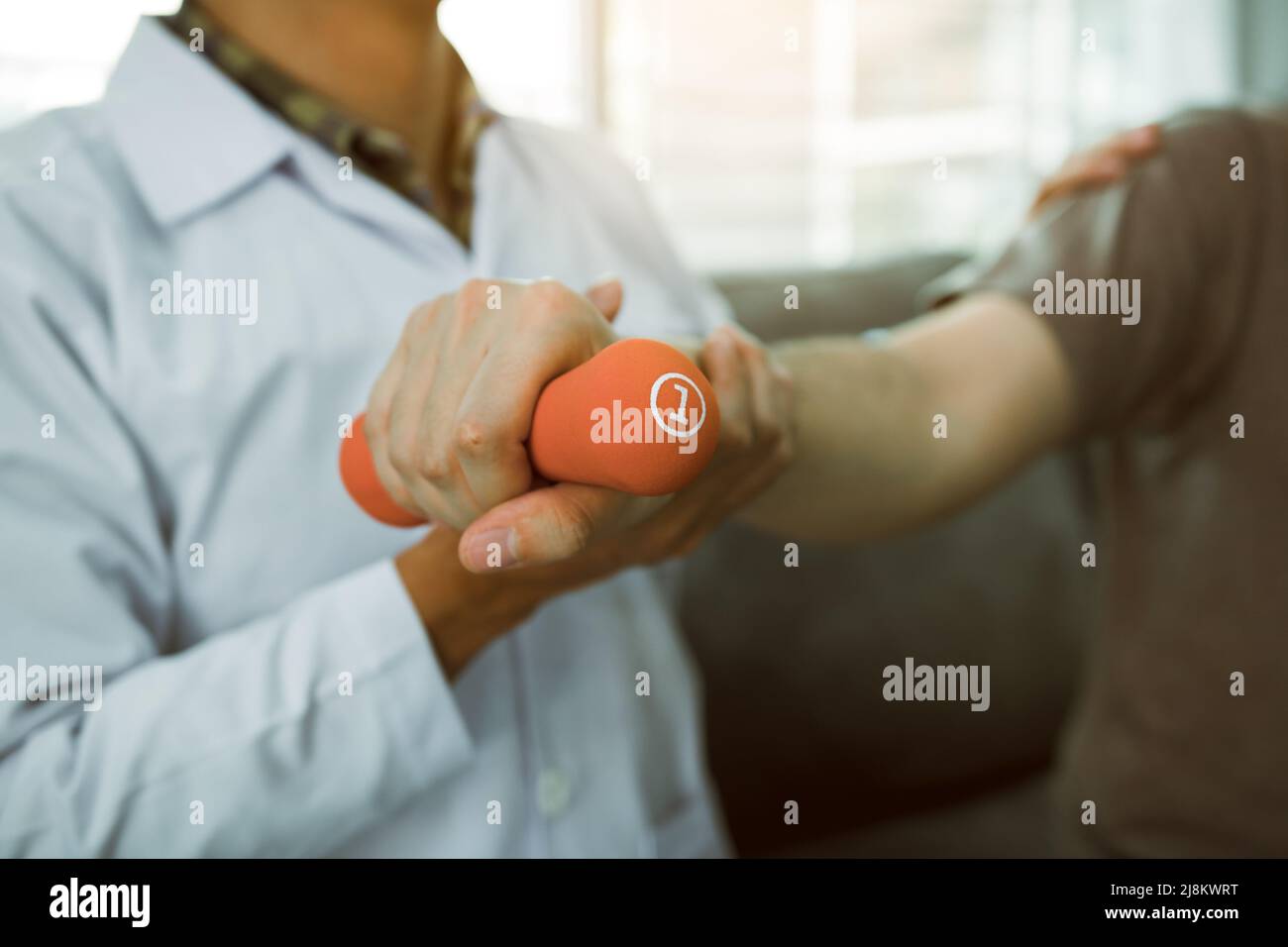 Asian physiotherapist helping a patient lifting dumbbells work through ...