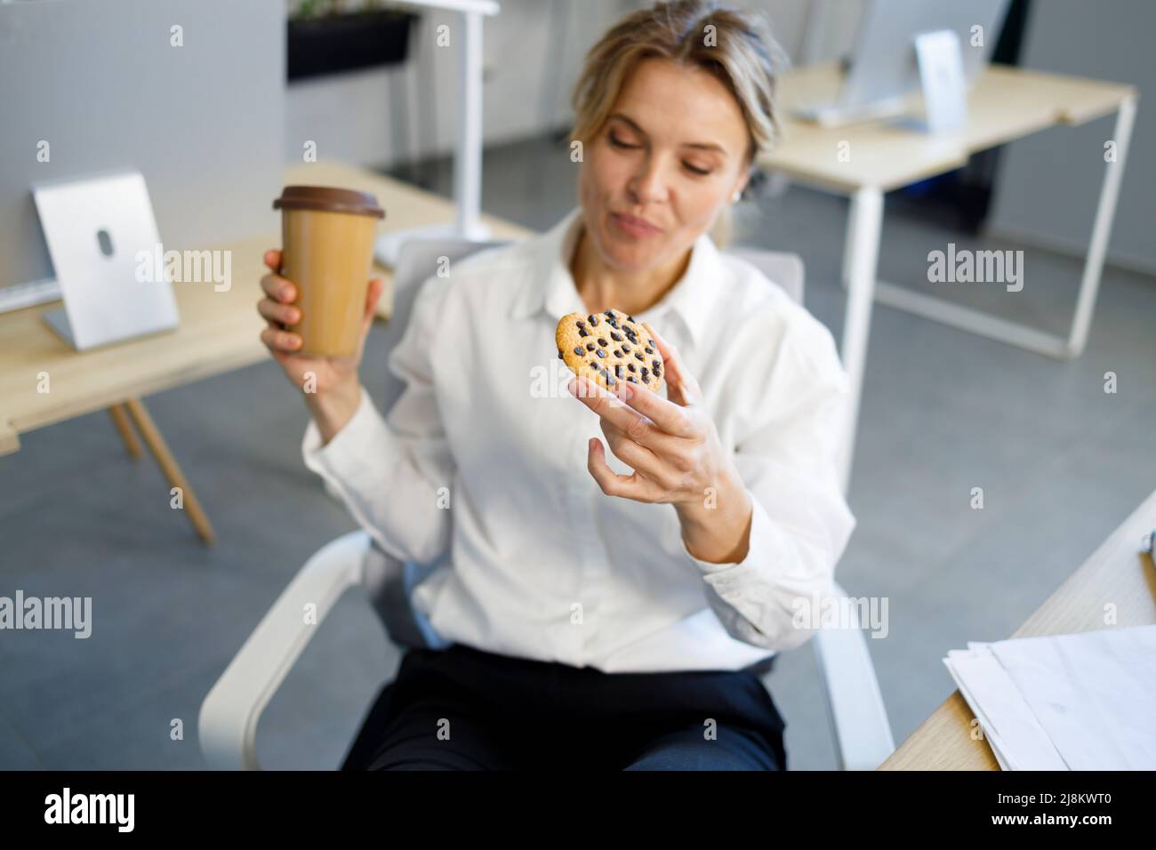 Business woman eating cookies and drinking coffee while having lunch at ...
