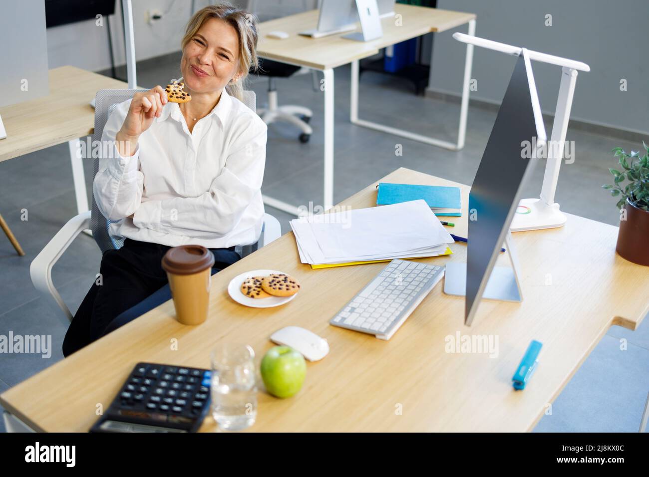 Adult female office worker eating cookies during coffee break Stock ...