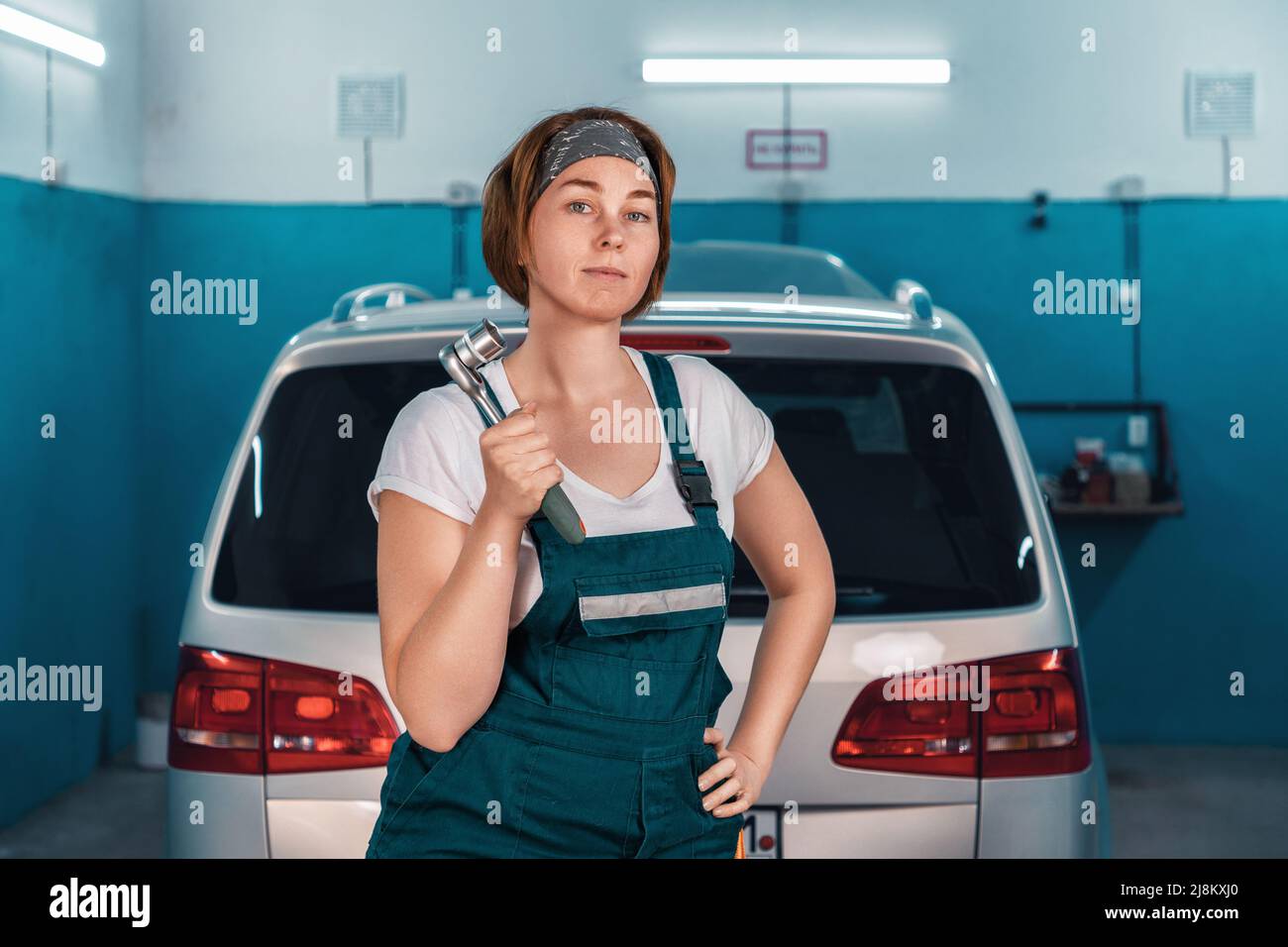 Young serious woman mechanic in overall and holding a wrench. At the ...