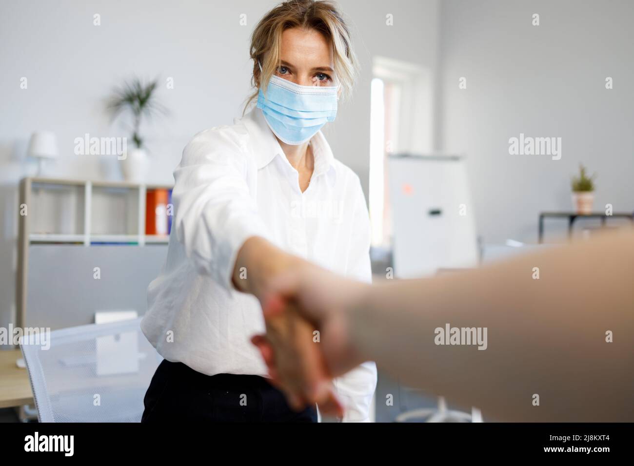 Female office worker in protective mask shaking hands of partner. Virus ...