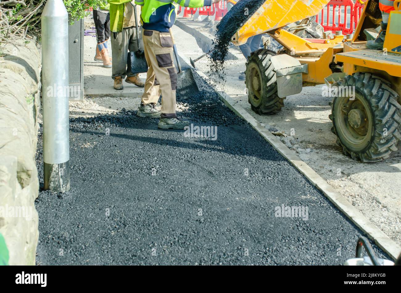 Construction workers placing hot tarmac during roadworks and footpath ...