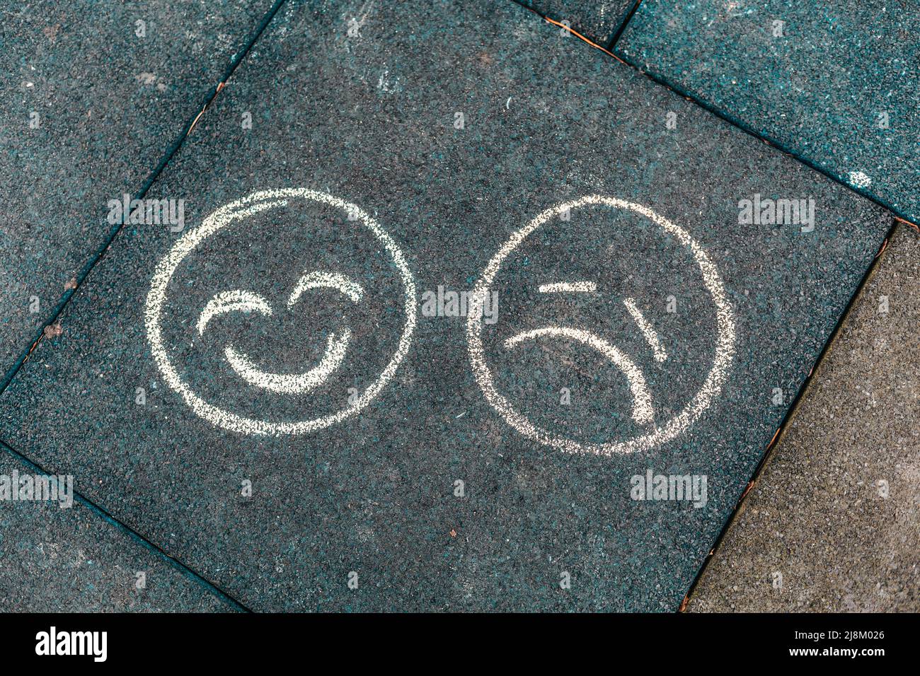 Smiling and sad emoji drawn with crayons on the ground. The concept of ...