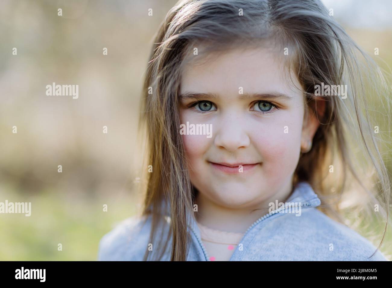 A portrait of pretty child girl standing in summer park looking in ...