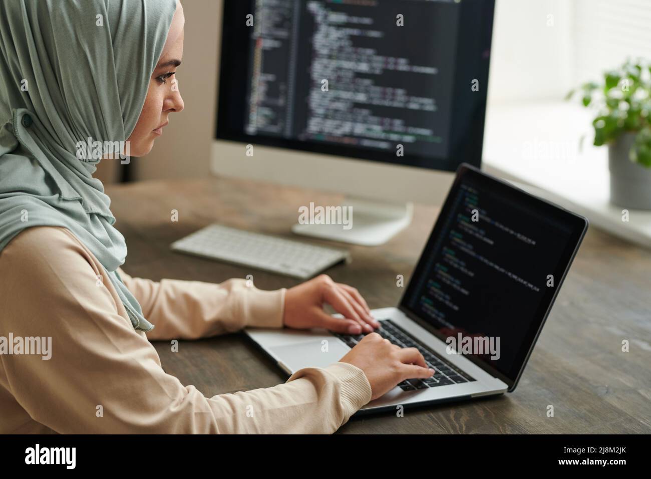 Professional programmer wearing hijab sitting at office table typing ...