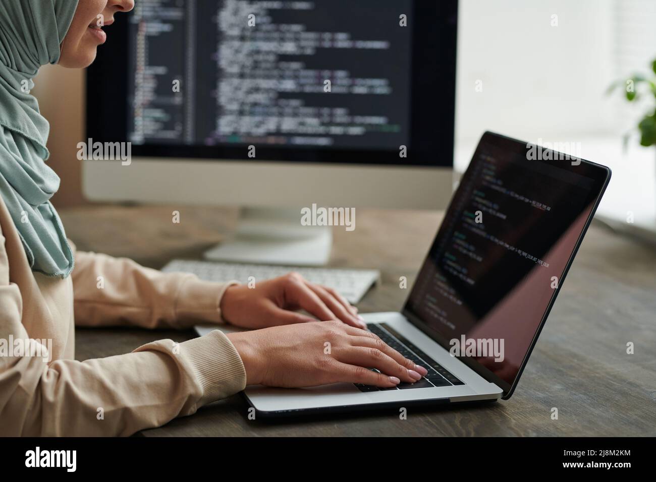 Unrecognizable professional programmer wearing hijab sitting at office table working on computer ...