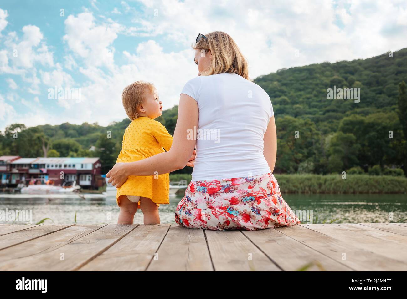 Summer vacation. A mother and cute baby sitting on the pier. Back view ...