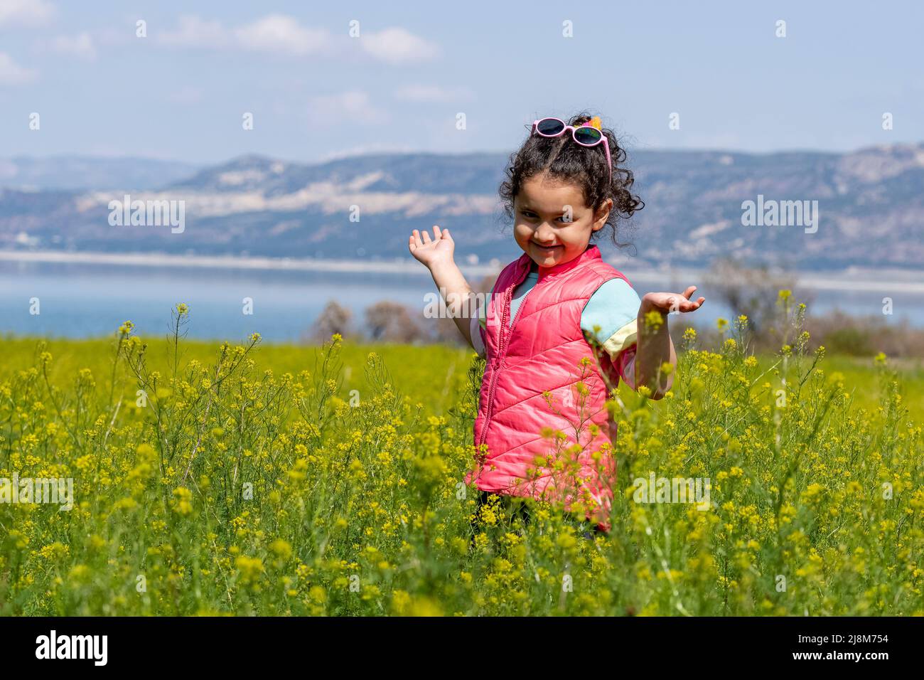 Selective focus of happy girl in pink dress walking through mustard ...