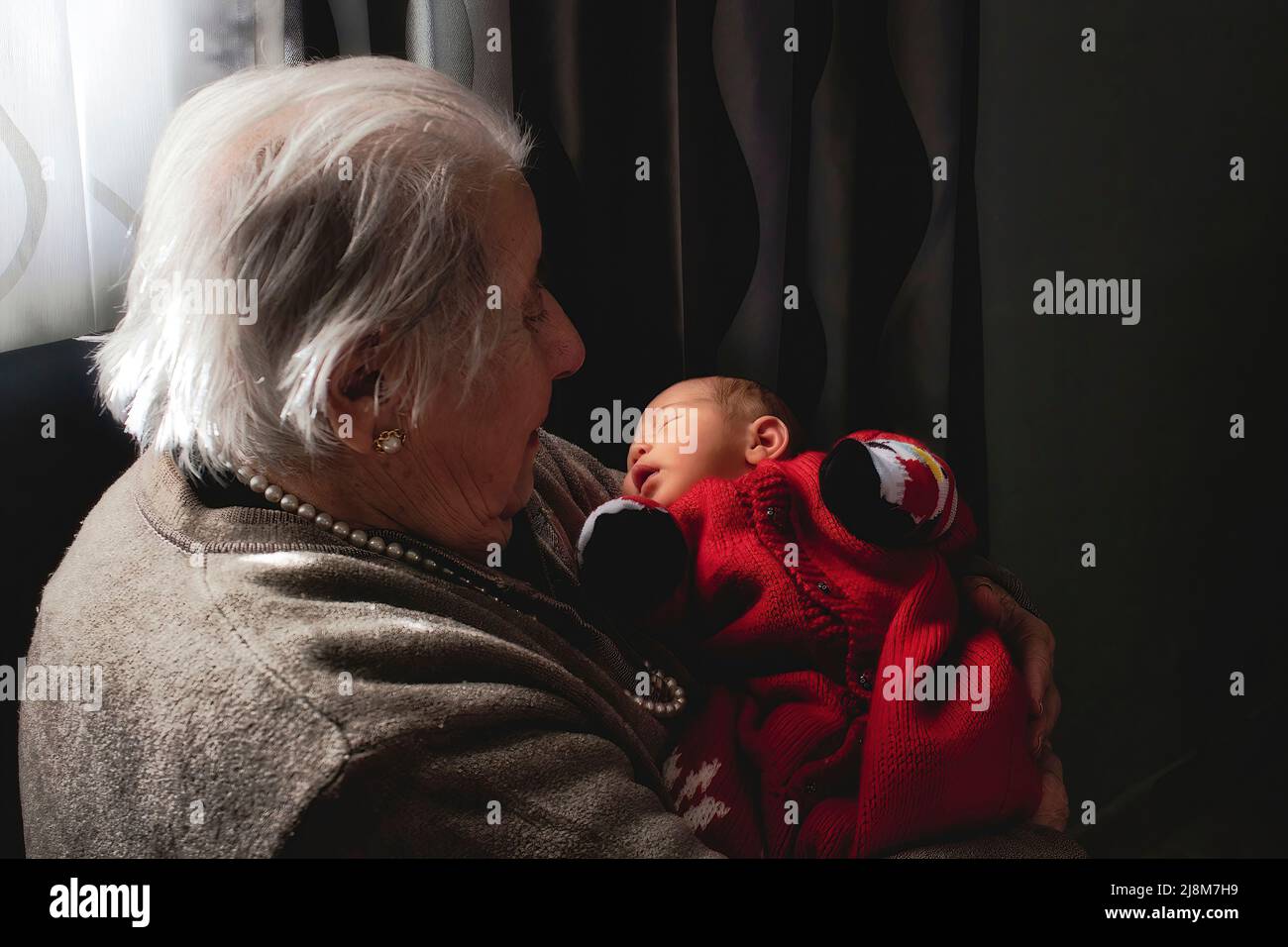 An old white-haired great-grandmother holding her newborn grandchild ...