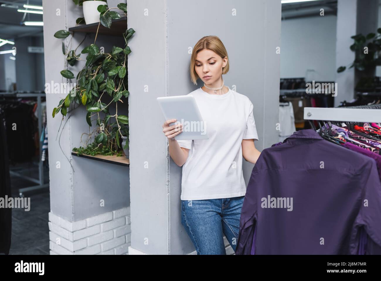 Blonde retailer using digital tablet near clothes in second hand Stock ...