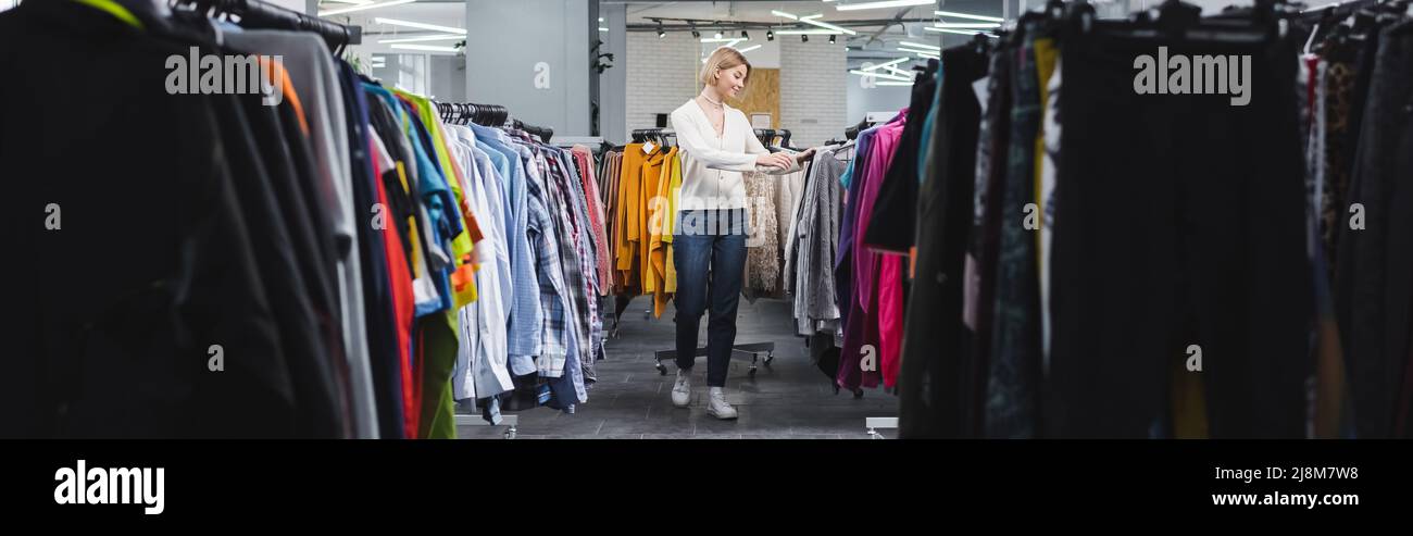 Side view of positive woman walking near clothes on hangers in vintage ...