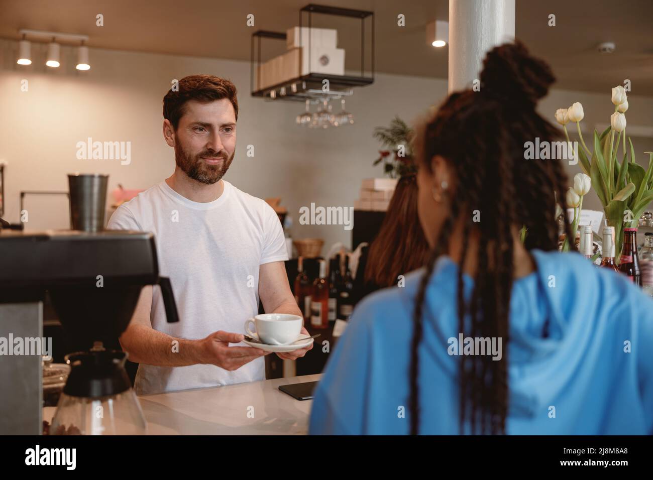 Cheerful handsome waiter serving coffee to female client at bar ...