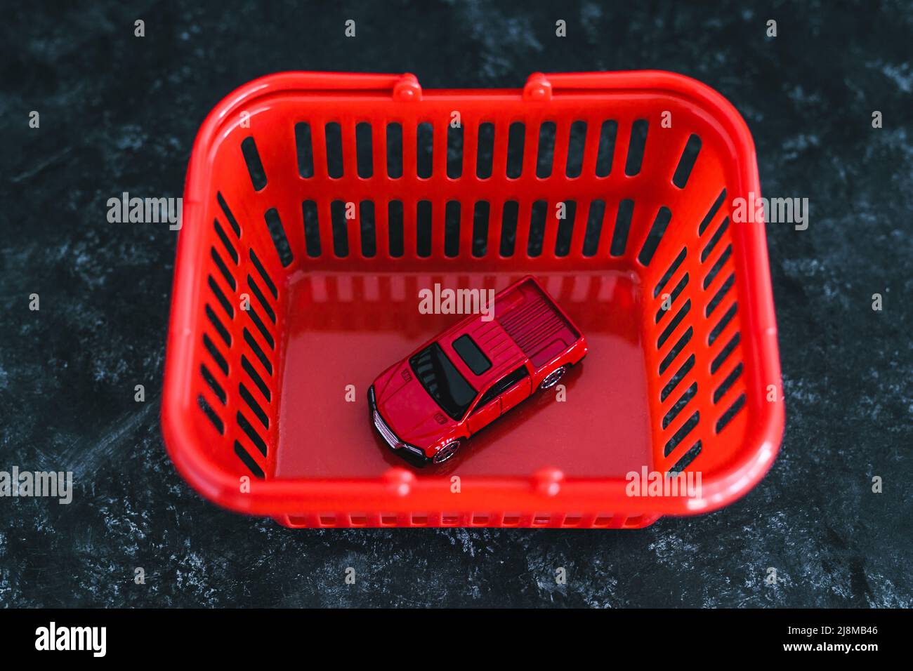 red toy car inside of shopping basket over black marble background ...