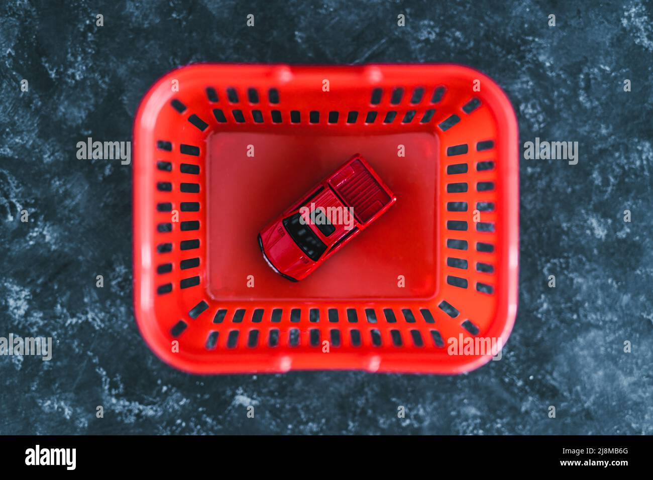 red toy car inside of shopping basket over black marble background ...