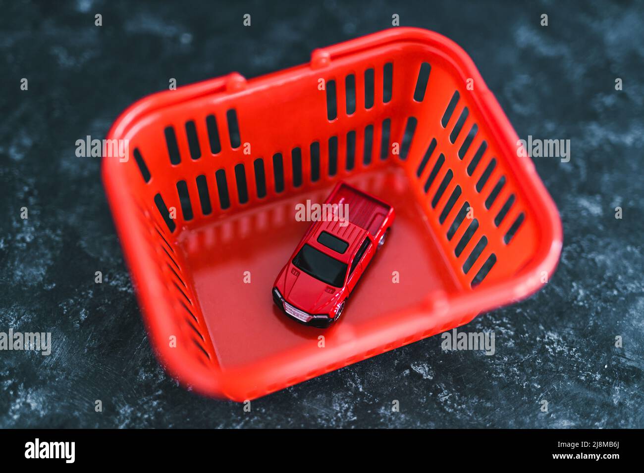 red toy car inside of shopping basket over black marble background ...