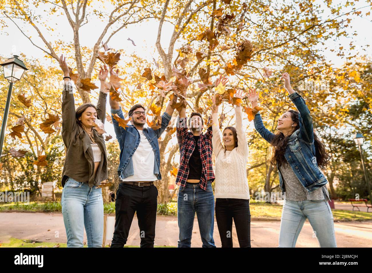 Group of friends in the park having fun throwing leaves in the air ...