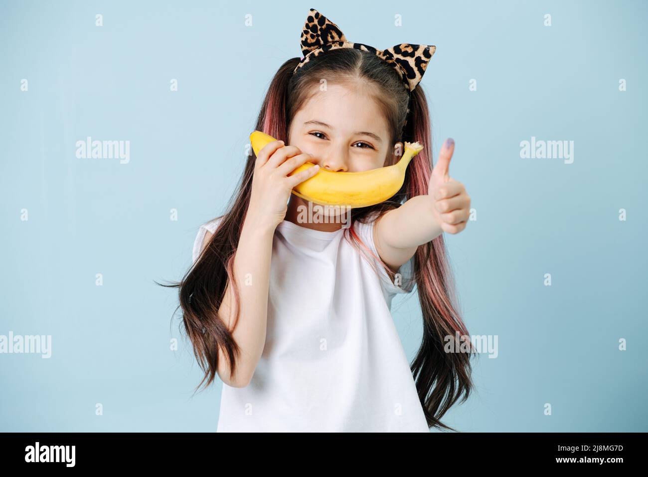 Positive Looking Tween Girl With Cat Ears Holding Banana Over Her Mouth