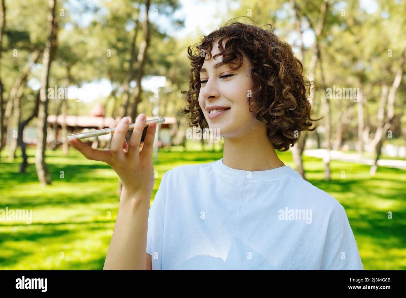 Smiling redhead woman wearing white tee talking on the phone speaker ...