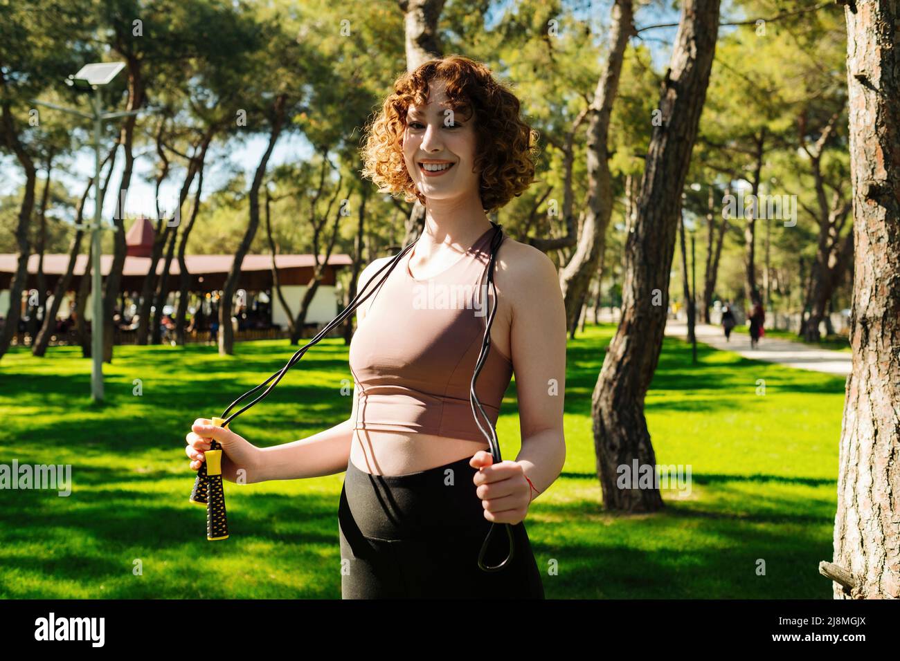 Sporty redhead young woman posing with a skipping rope around her neck ...