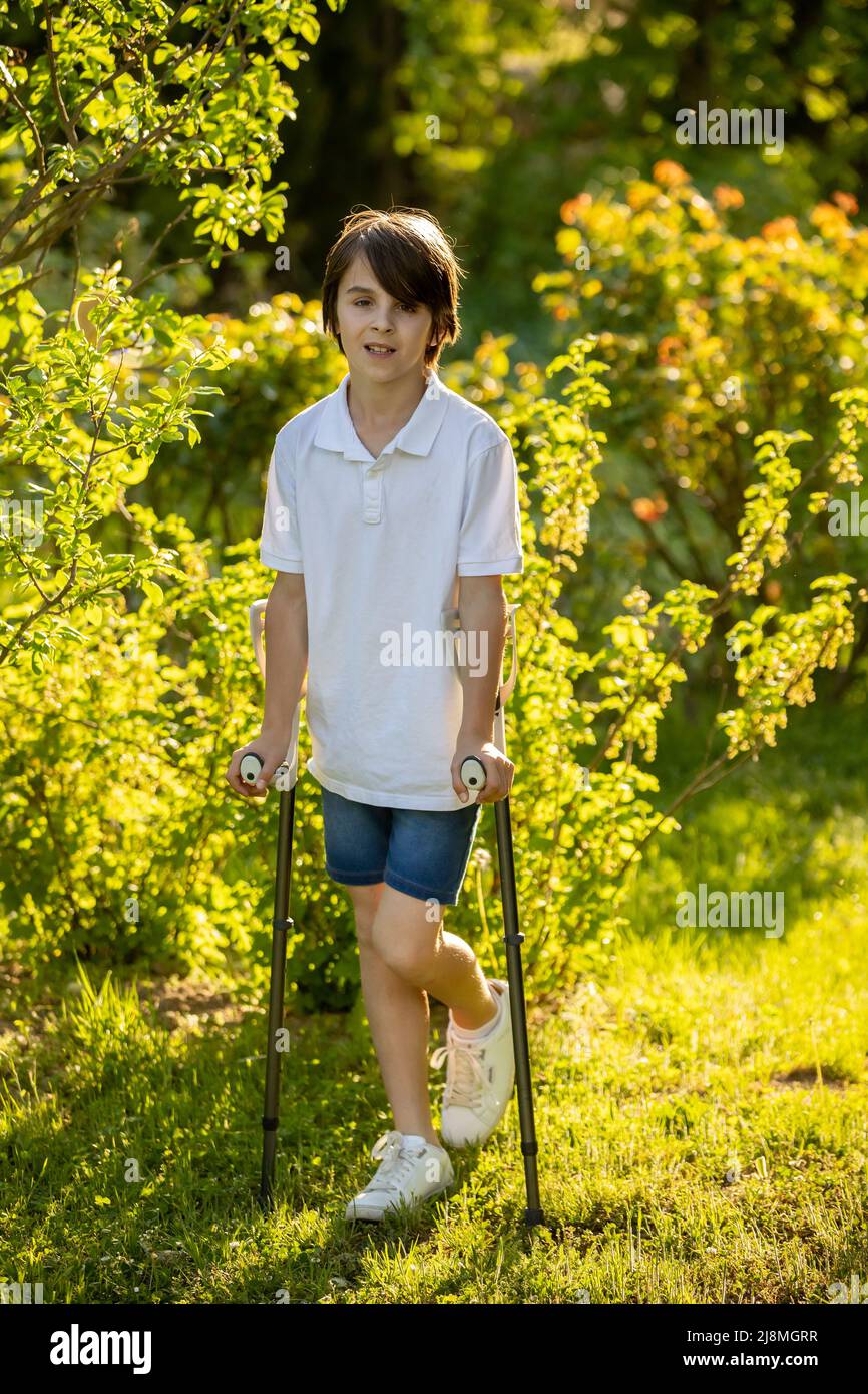 Cute child, boy, walking with crutches in a garden, having his leg ...