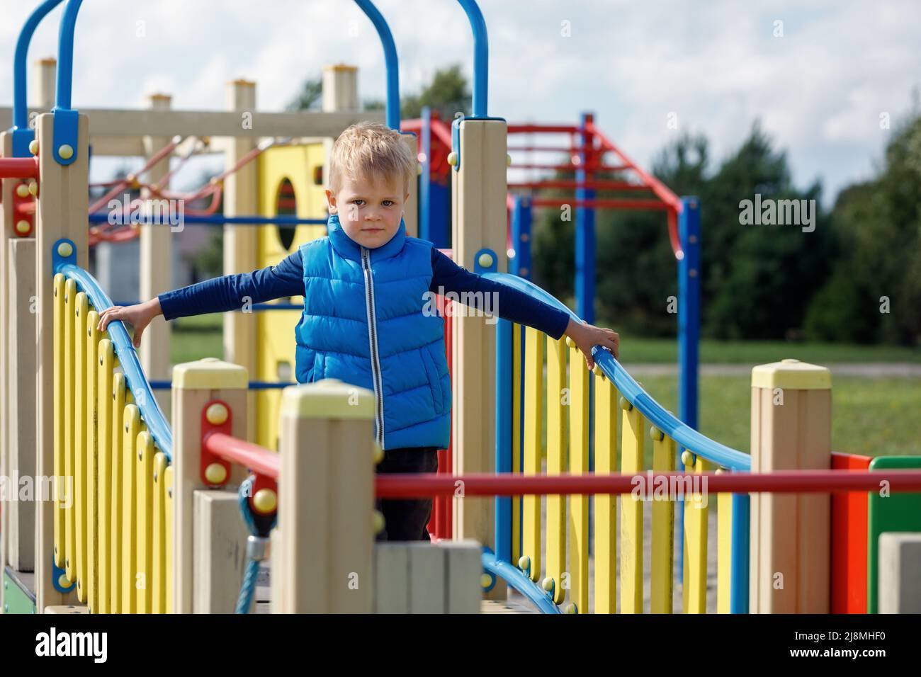 A cute, blond child walks in the modern colorful outdoor playground ...