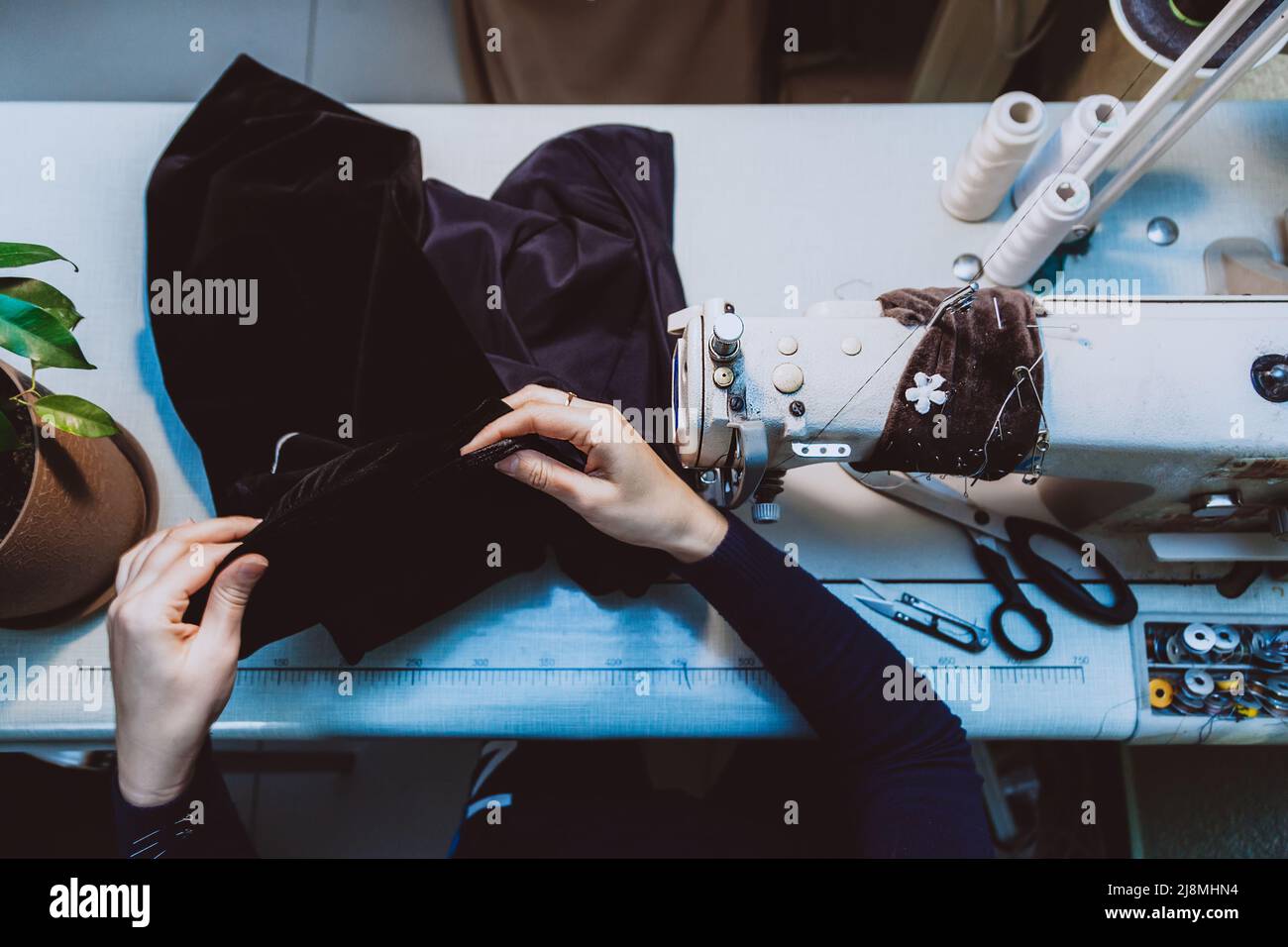 A woman tailor sews clothes - a fashionable jacket made of velvet ...