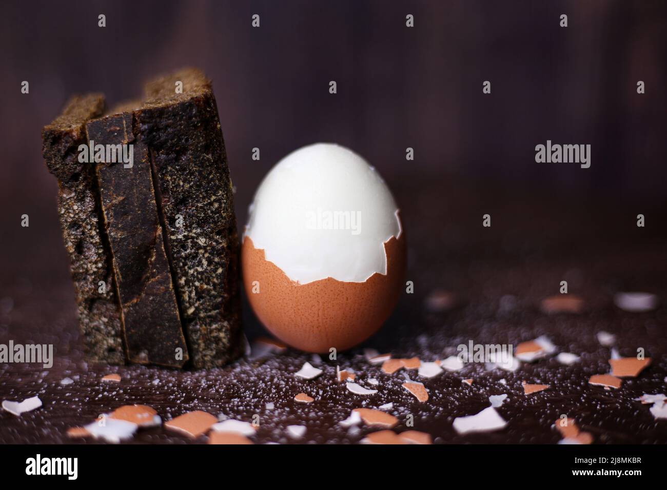 Brown boiled half-peeled egg and pieces of black bread on a dark wooden ...