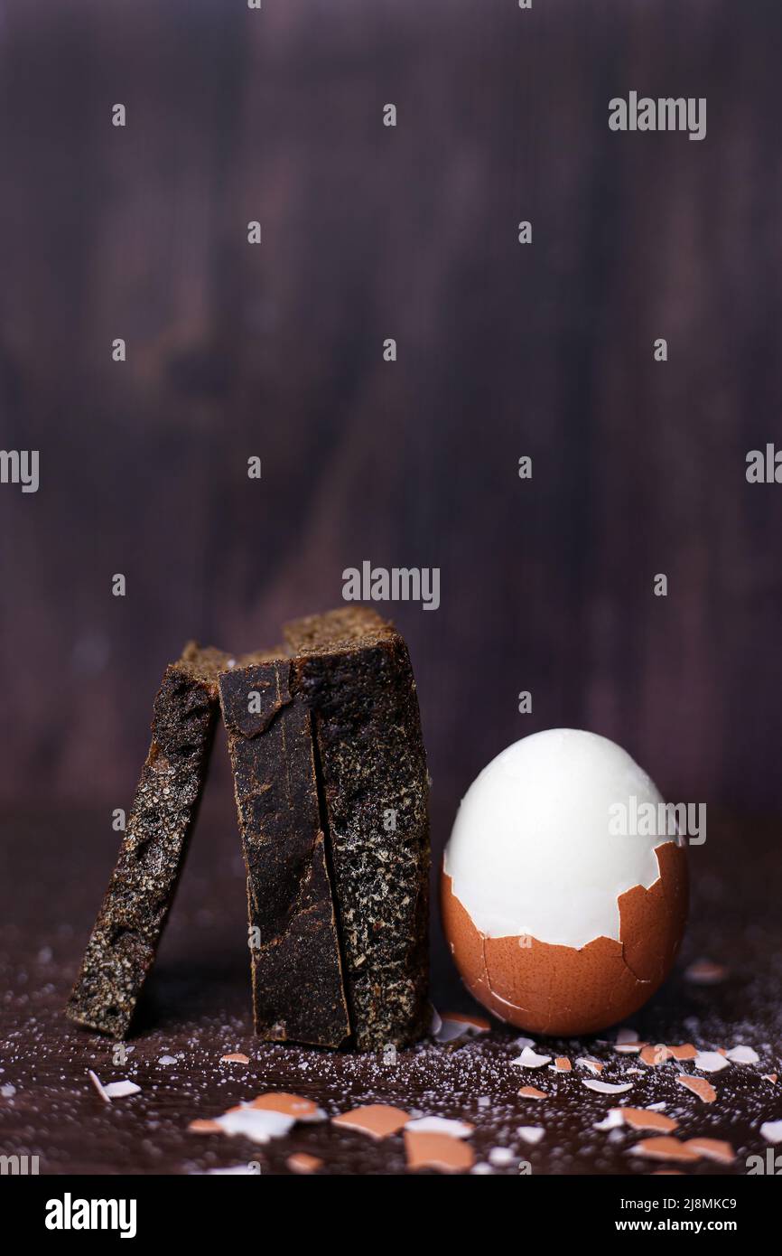 Brown boiled half-peeled egg and pieces of black bread on a dark wooden ...