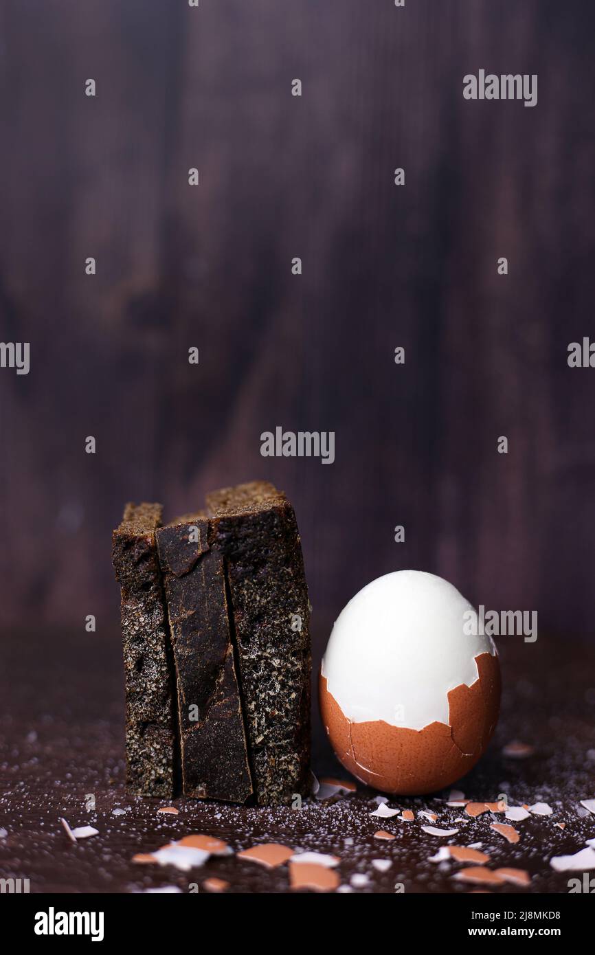 Brown boiled half-peeled egg and pieces of black bread on a dark wooden ...
